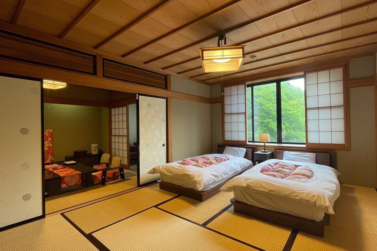 Quarto japonês tradicional com tatames, duas camas, uma porta deslizante e vista para o verde lá fora.