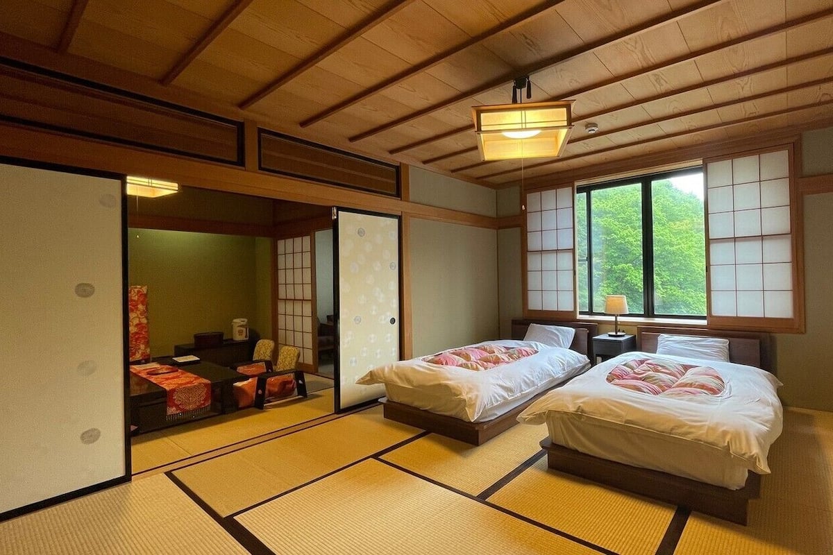 Quarto tradicional japonês com tatames, duas camas, uma porta deslizante e vista para o verde lá fora.