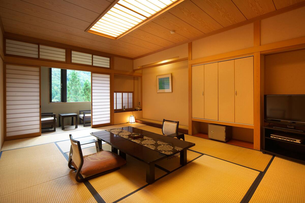 Quarto japonês tradicional com tatames, uma mesa baixa com almofadas, portas deslizantes e uma televisão.