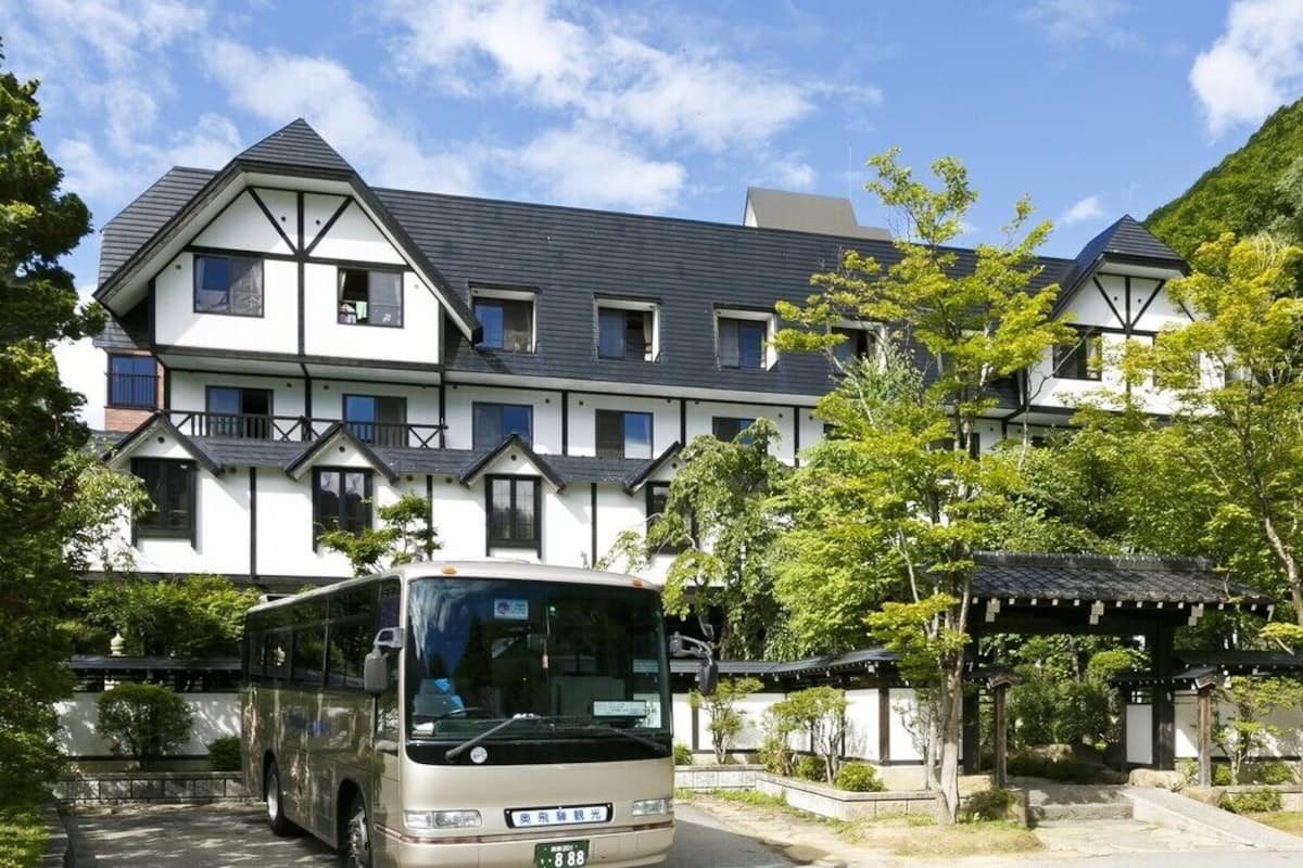 Um edifício de vários andares com um ônibus estacionado na frente, rodeado por vegetação e arquitetura tradicional.