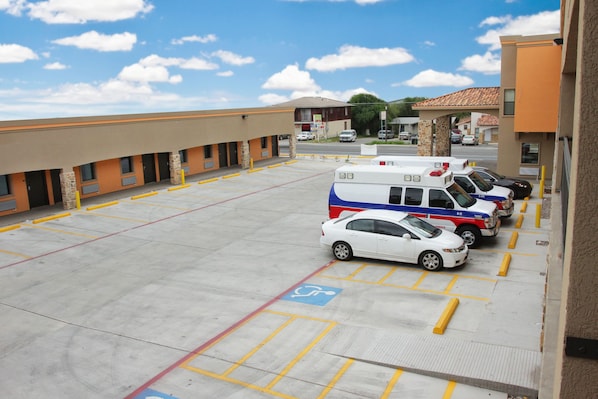 Um estacionamento com vários carros e uma ambulância, um prédio com várias portas e um céu claro.