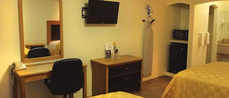 Quarto de hotel com duas camas, uma escrivaninha com cadeira, televisão, espelho, guarda-roupa e área de duche.