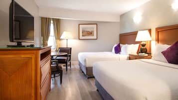 Quarto de hotel com duas camas, uma escrivaninha, televisão e uma luminária.