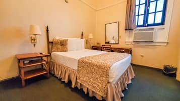 Quarto de hotel com cama, mesas de cabeceira, escrivaninha, espelho e janela com cortinas.