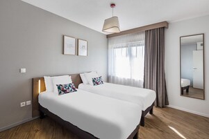 Quarto de hotel com duas camas, um espelho grande e uma janela com cortinas.