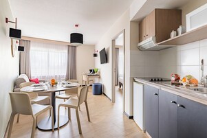 Cozinha moderna com fogão embutido, pia e armários. Há uma área de jantar com mesa redonda e cadeiras, e uma janela com cortinas.