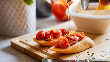 Duas fatias de torradas cobertas de tomate e ervas, com uma faca e uma tigela em tábua de madeira.