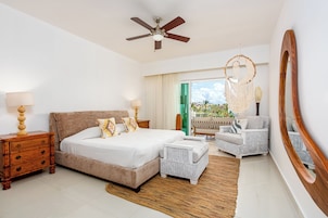 Quarto com cama, mesas de cabeceira, ventilador de teto, espelho grande e vista através de uma porta de vidro.