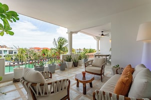 Ampla área de estar externa com vista para uma piscina e edifícios ao fundo.