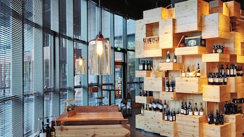 Um interior moderno com estantes de madeira exibindo garrafas de vinho, uma mesa de madeira e luminárias pendentes.