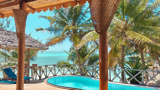 Área na piscina com um telhado de palha, espreguiçadeiras e vista para o oceano.