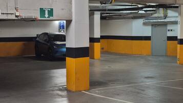 Garagem subterrânea de estacionamento com pilares amarelos e pretos, um carro azul estacionado e uma placa de estacionamento verde.