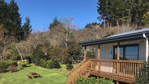 Uma cabana com deck de madeira, uma pequena escadaria e um gramado com uma mesa para piquenique.