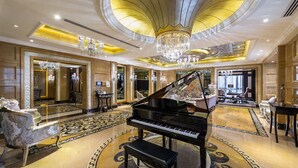 Um hall imponente com um piano de cauda, lustres elaborados e um tapete luxuoso.