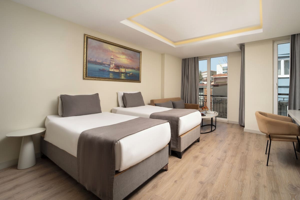 Quarto de hotel com duas camas, uma escrivaninha, uma cadeira, uma mesinha e um quadro na parede.