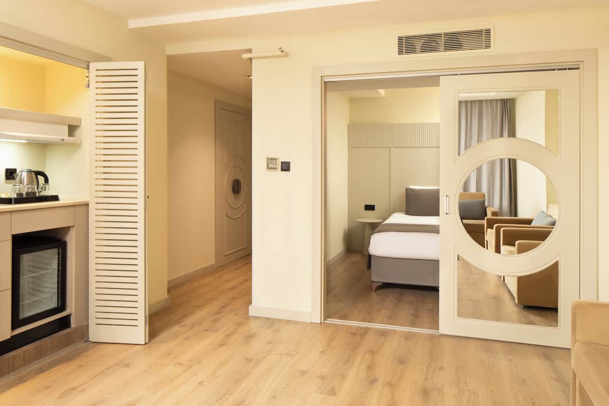 Quarto de hotel moderno com cozinha compacta, cama, área de estar e um espelho grande.