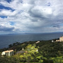 Paisagem costeira com vista para o mar, uma colina com edifícios e céu parcialmente nublado.