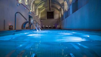 Piscina interior com água cristalina, chão ladrilhado e teto com claraboias.