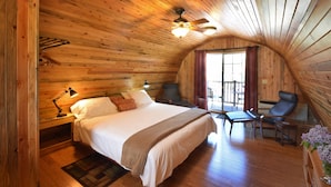 Um quarto acolhedor em cabana de madeira, com uma cama, mesas de cabeceira, escrivaninha e uma cadeira.