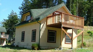 Uma casa de dois andares com varanda, telhado verde e fachada amarelo claro.