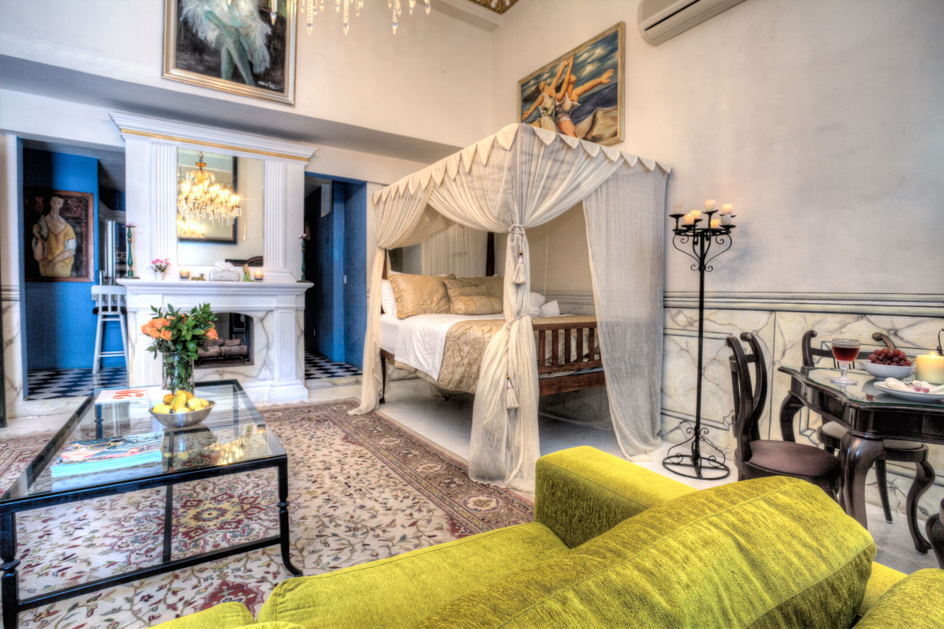 Quarto com cama de dossel, mesa de centro de vidro, mesa de jantar com cadeiras e um candelabro.