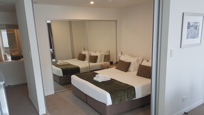 Quarto de hotel com duas camas, um espelho grande e uma mesinha de cabeceira.