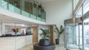 Um lobby moderno com uma mesa de recepção, área de estar e um elevador de vidro.
