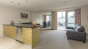 Cozinha moderna com ilha central, área de jantar com mesa e cadeiras e sala de estar com sofá e uma janela grande.