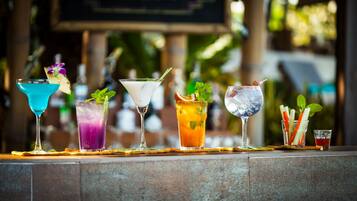 Um balcão de bar com diversos coquetéis coloridos, guarnições e um pequeno copo de bebida vermelha.