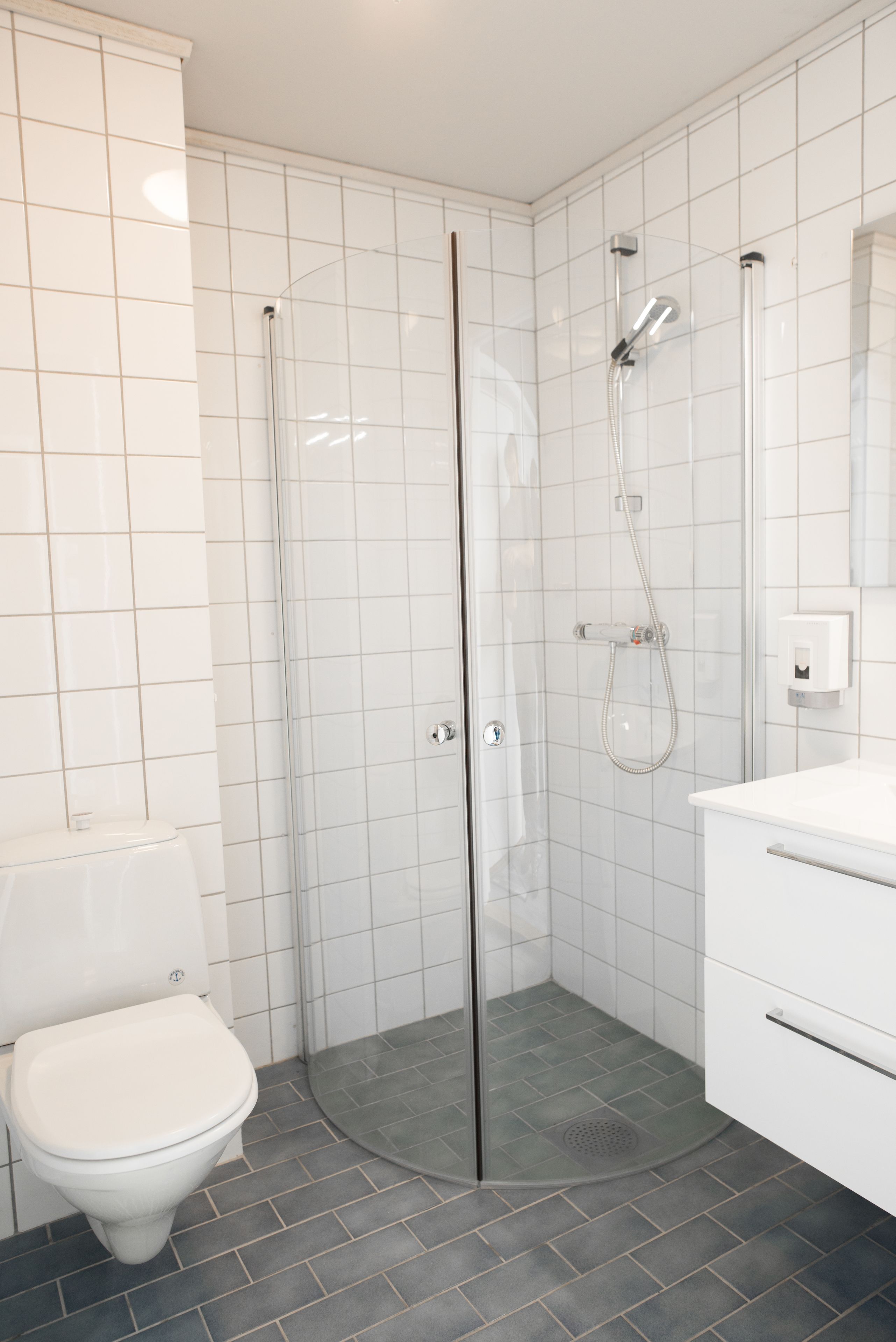 Um banheiro moderno com chuveiro em vidro, azulejos brancos e vaso sanitário branco.