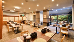 Uma ampla área de refeições com várias mesas e cadeiras, apresentando decoração tradicional japonesa e vista para o exterior com vegetação.