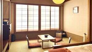 Um quarto japonês tradicional com tatames, uma mesa baixa, duas cadeiras e um amplo janelão com tela shoji.