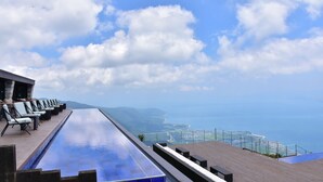 Piscina infinita no terraço com espreguiçadeiras e vista para o oceano.
