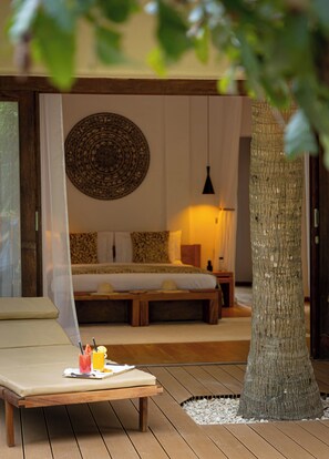 Quarto com cama, mesa de cabeceira e um tronco de árvore grande em primeiro plano.
