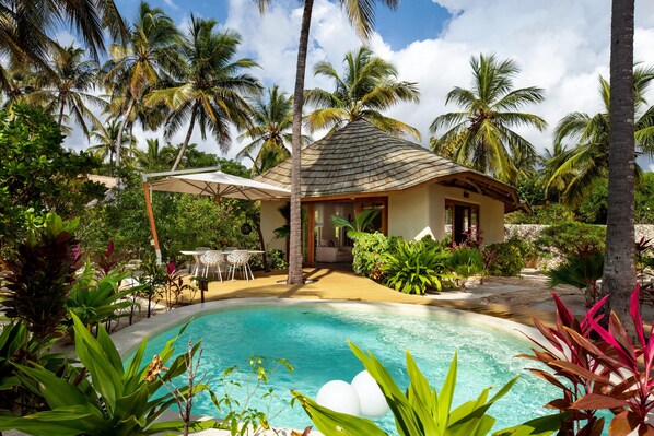 Um resort tropical com piscina, palmeiras e um edifício com telhado de palha.