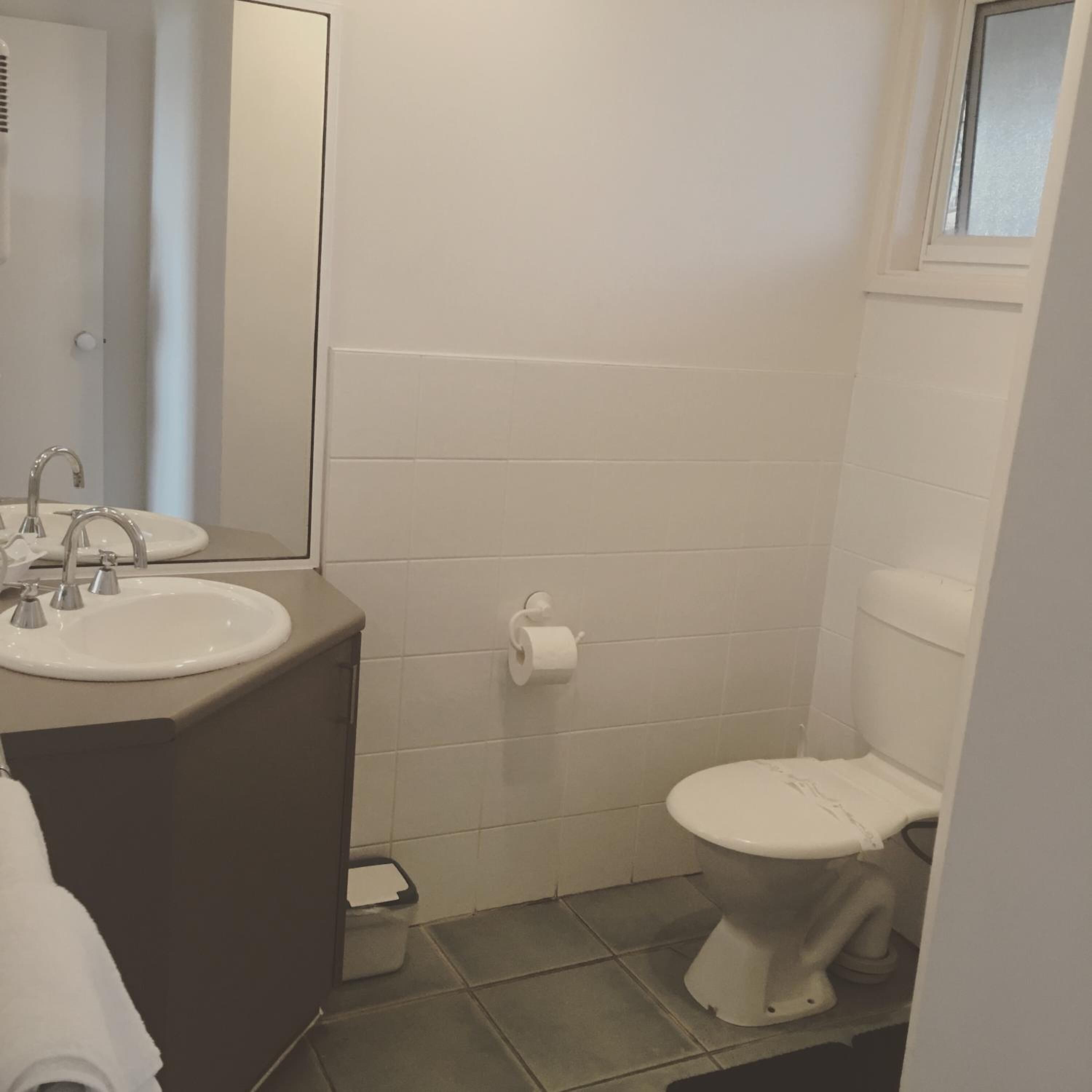 Uma casa de banho pequena e limpa, com lavatório, sanita e espelho.