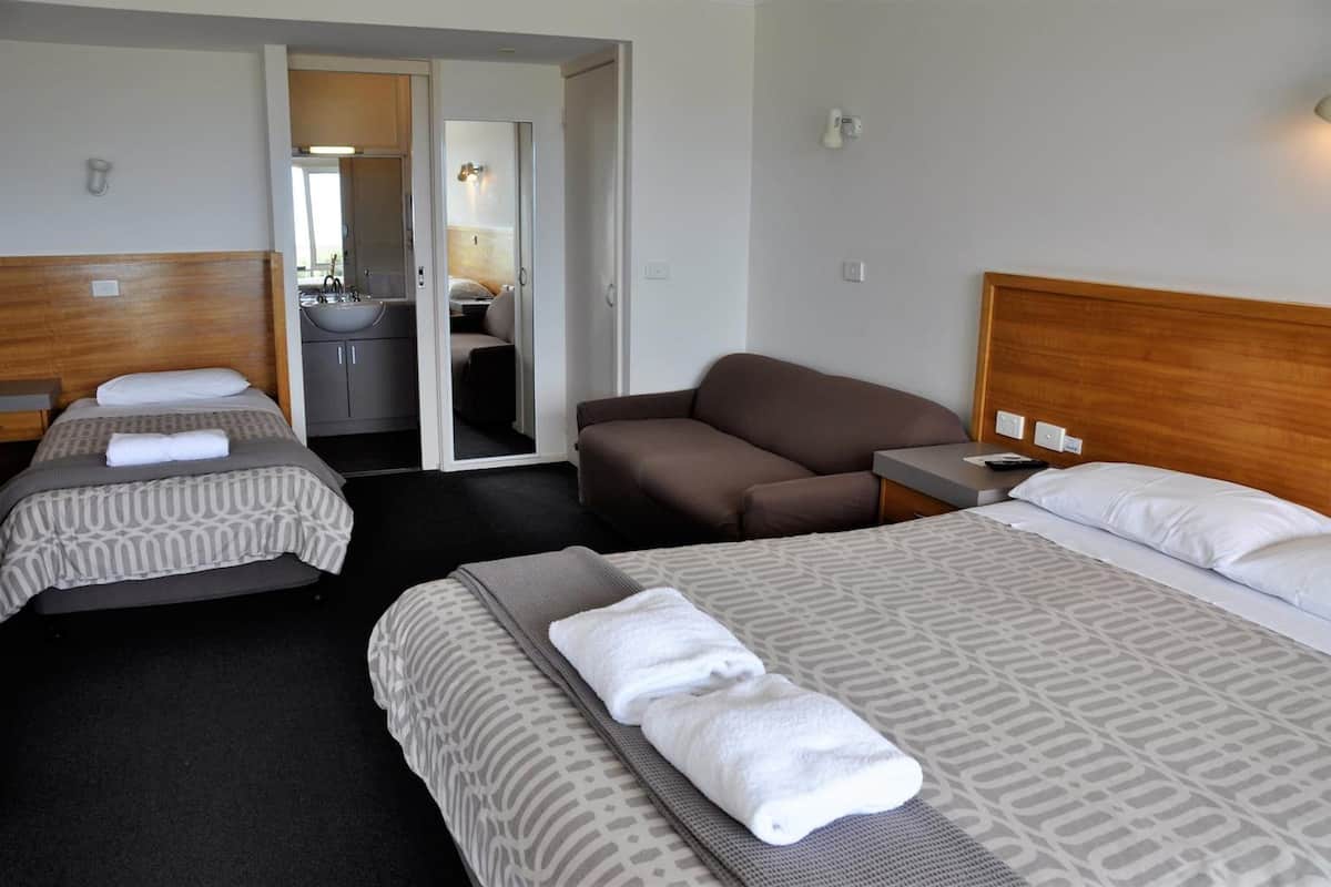 Quarto de hotel com duas camas, um sofá, uma mesinha e um banheiro visível por uma porta aberta.