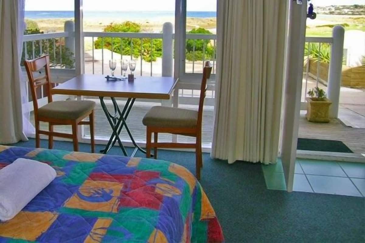 Quarto com cama, mesa e cadeiras, e vista para a praia.