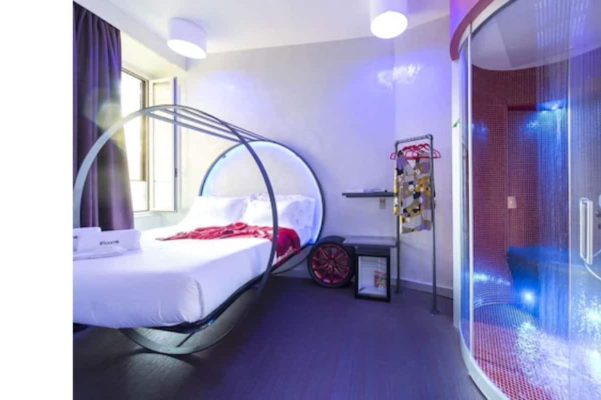 Quarto de hotel moderno com uma cama, uma janela circular e área de chuveiro.