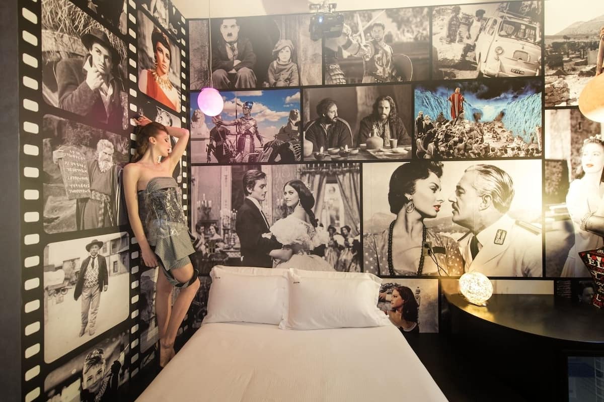 Um quarto com uma cama, uma parede com design de faixa de filme e várias fotografias emolduradas.