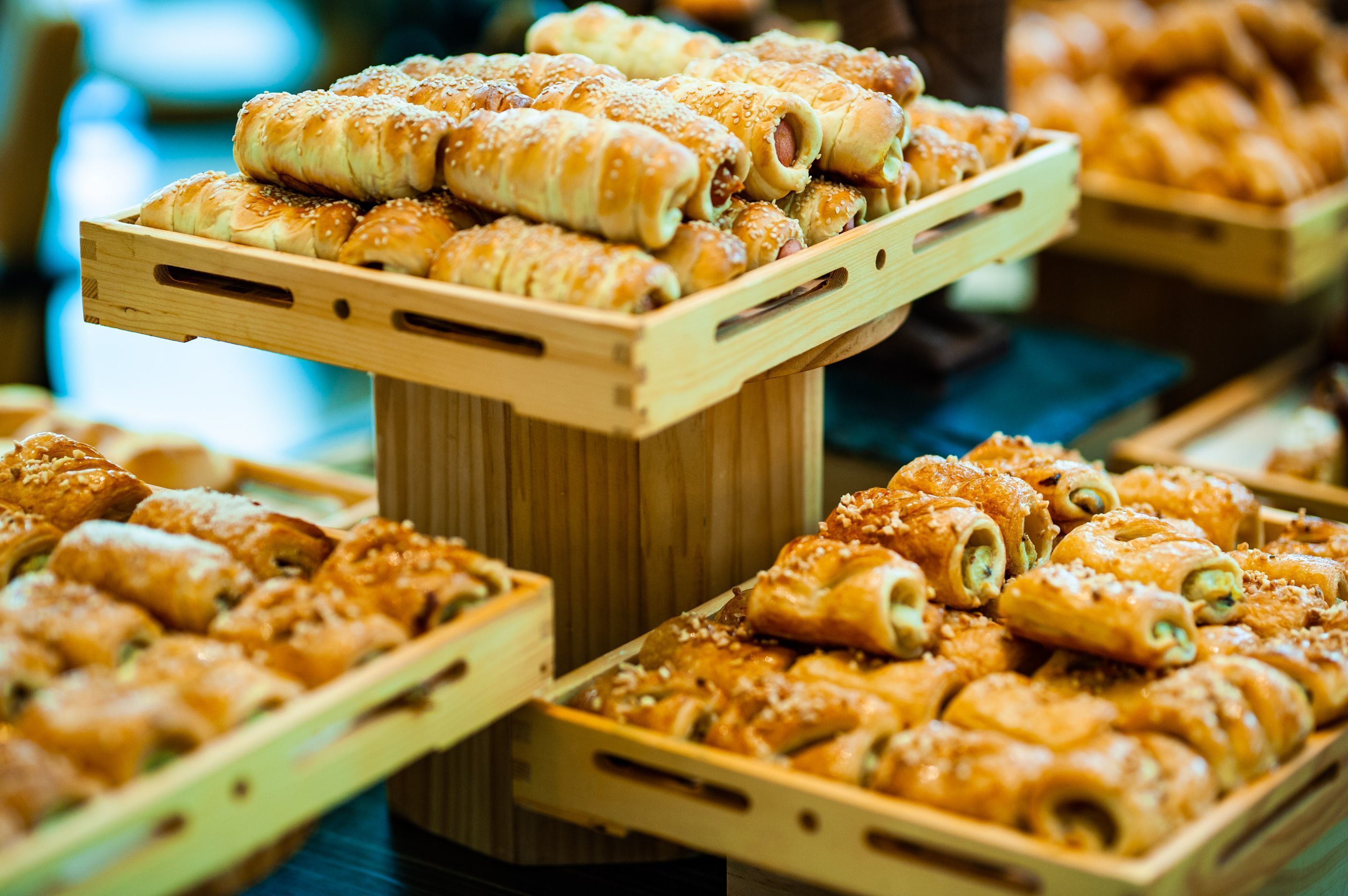 Exposição de diversos produtos de panificação, incluindo pães e doces, dispostos em suportes de madeira.