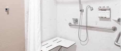 Área de chuveiro com barra de apoio, chuveiro manual e painel de controle fixado na parede.