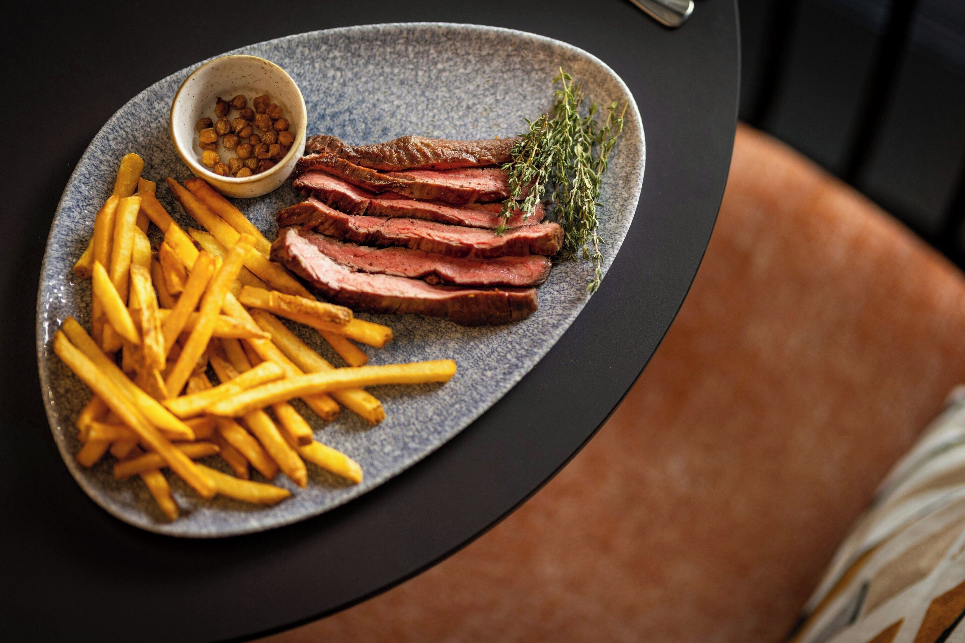 Prato com bife, batatas fritas e uma pequena tigela de acompanhamentos.