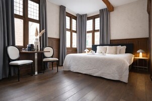 Quarto de hotel com uma cama grande, uma escrivaninha com cadeira e uma janela com cortinas.