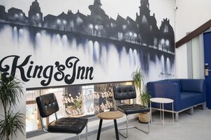 Área de recepção do King’s Inn com um grande mural, duas poltronas de couro, uma mesinha redonda e um sofá azul.