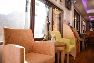 Uma área de estar com cadeiras acolchoadas e uma pequena mesa, um sapato decorativo sobre a mesa, e vista para o exterior através de uma janela.