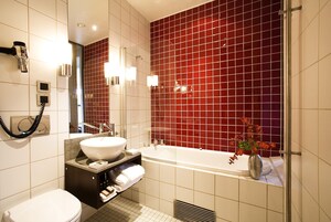 Casa de banho moderna com sanita branca, lavatório, banheira e paredes com azulejos vermelhos.