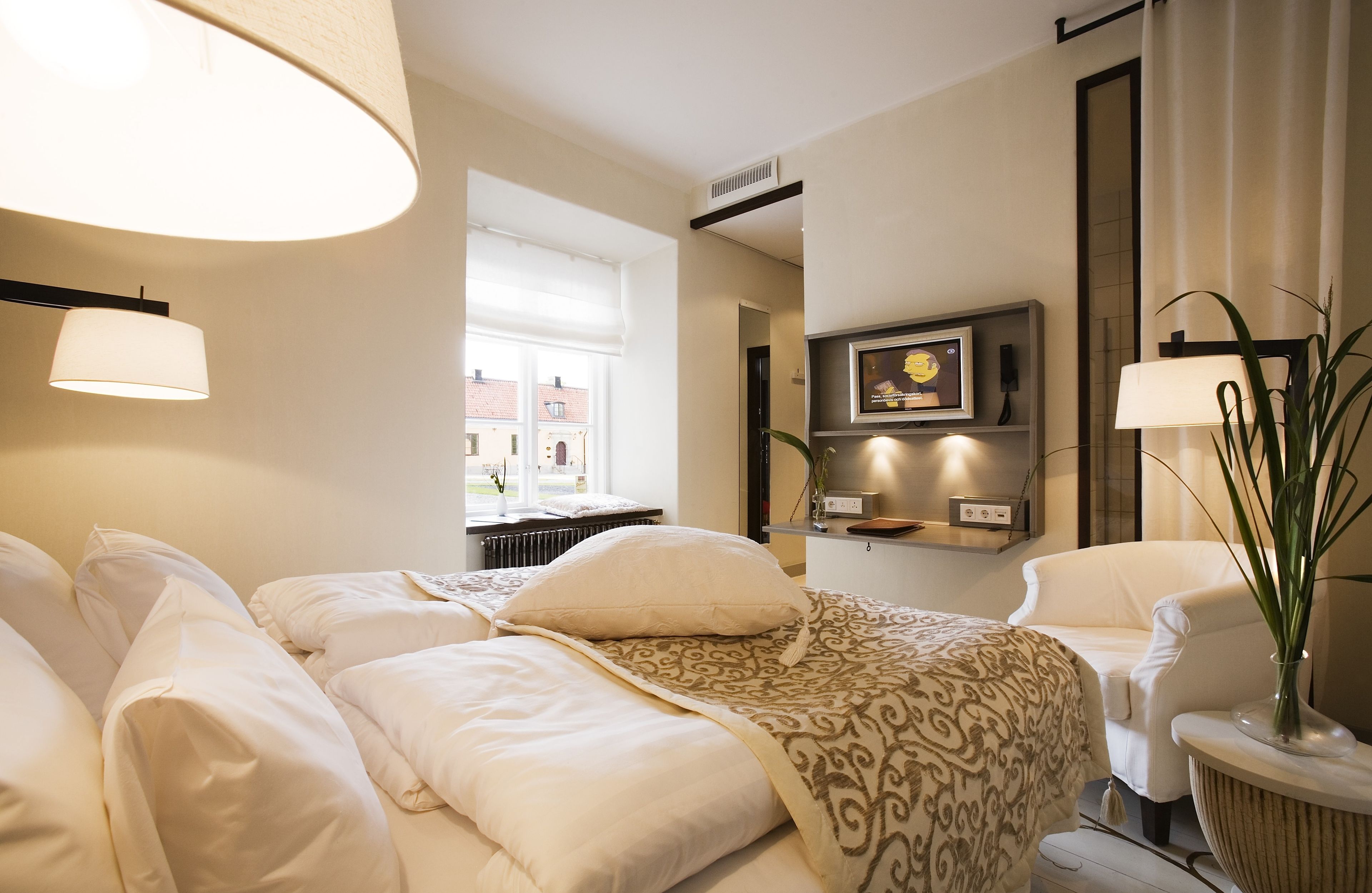Quarto de hotel com cama, poltrona, luminária e janela.