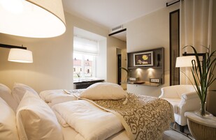Quarto de hotel com cama, poltrona, luminária e janela.