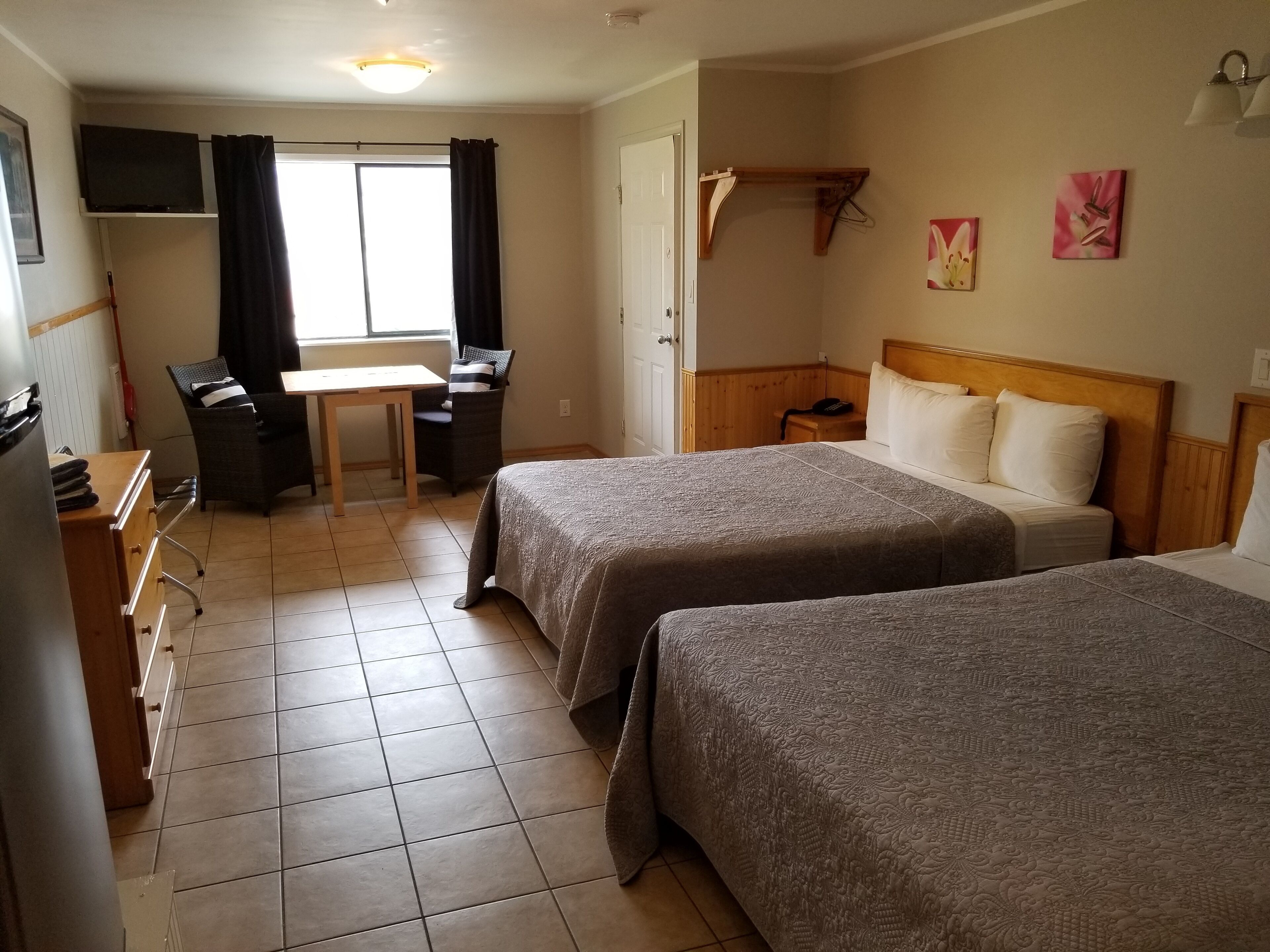 Quarto de hotel com duas camas, uma escrivaninha, uma cadeira, uma televisão e uma janela com cortinas.